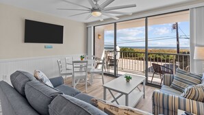 Uma sala de estar moderna com ventilador de teto, TV de tela plana e varanda com vista para a praia.