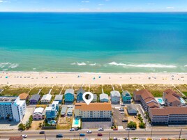 Vista aérea de um hotel à beira-mar, com vários edifícios, uma praia ao fundo e uma visão ampla do oceano.