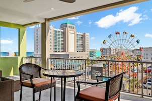 Varanda com cadeiras de vime e uma mesa, com vista para uma roda gigante e um horizonte urbano com edifícios altos.