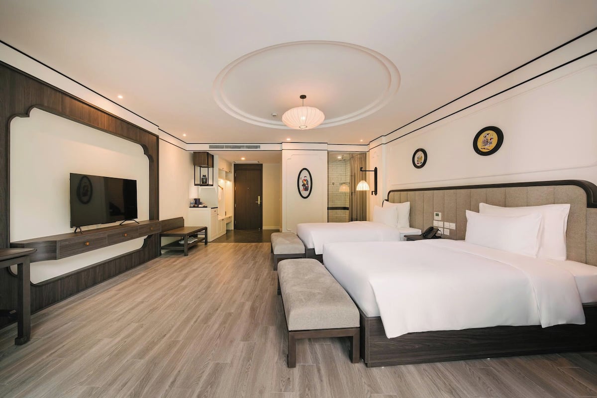 Quarto de hotel com uma cama grande, televisão, escrivaninha e um banco.