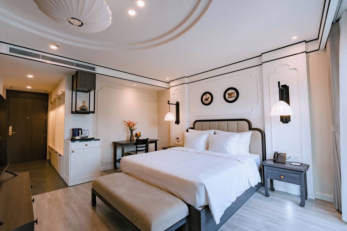 Quarto de hotel moderno com uma cama grande, mesas de cabeceira, uma escrivaninha e um guarda-roupa.