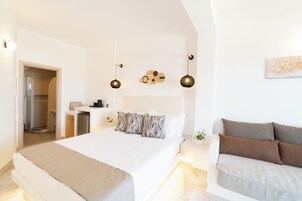 Quarto de hotel moderno com uma cama grande, um sofá, uma escrivaninha e um banheiro visível por uma porta aberta.