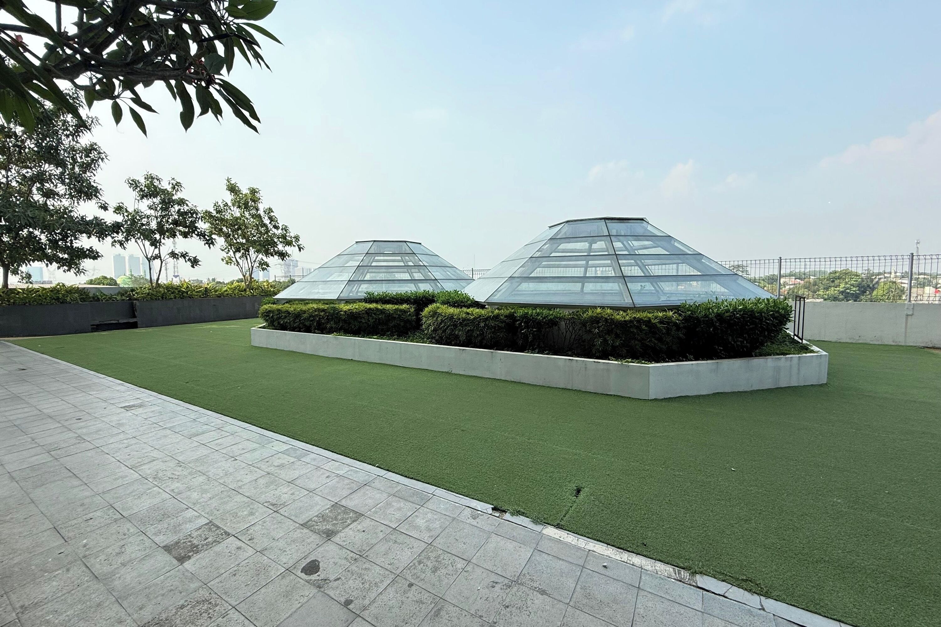 Um jardim no terraço com duas estufas de vidro, rodeado por um caminho pavimentado e ladeado por sebes baixas.
