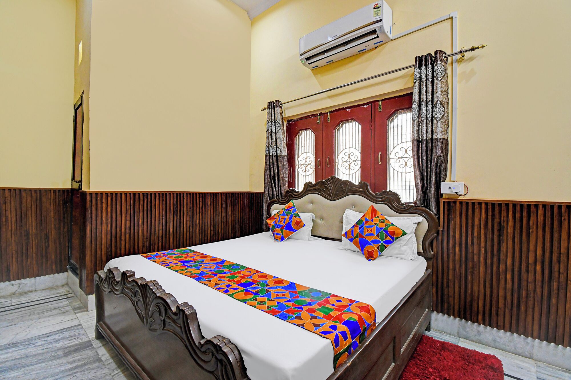 Um quarto com uma cama, uma porta vermelha, um ar condicionado e uma janela com cortinas.