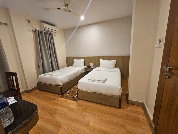 Quarto de hotel com duas camas, ventoinha no teto, ar condicionado e piso de madeira.