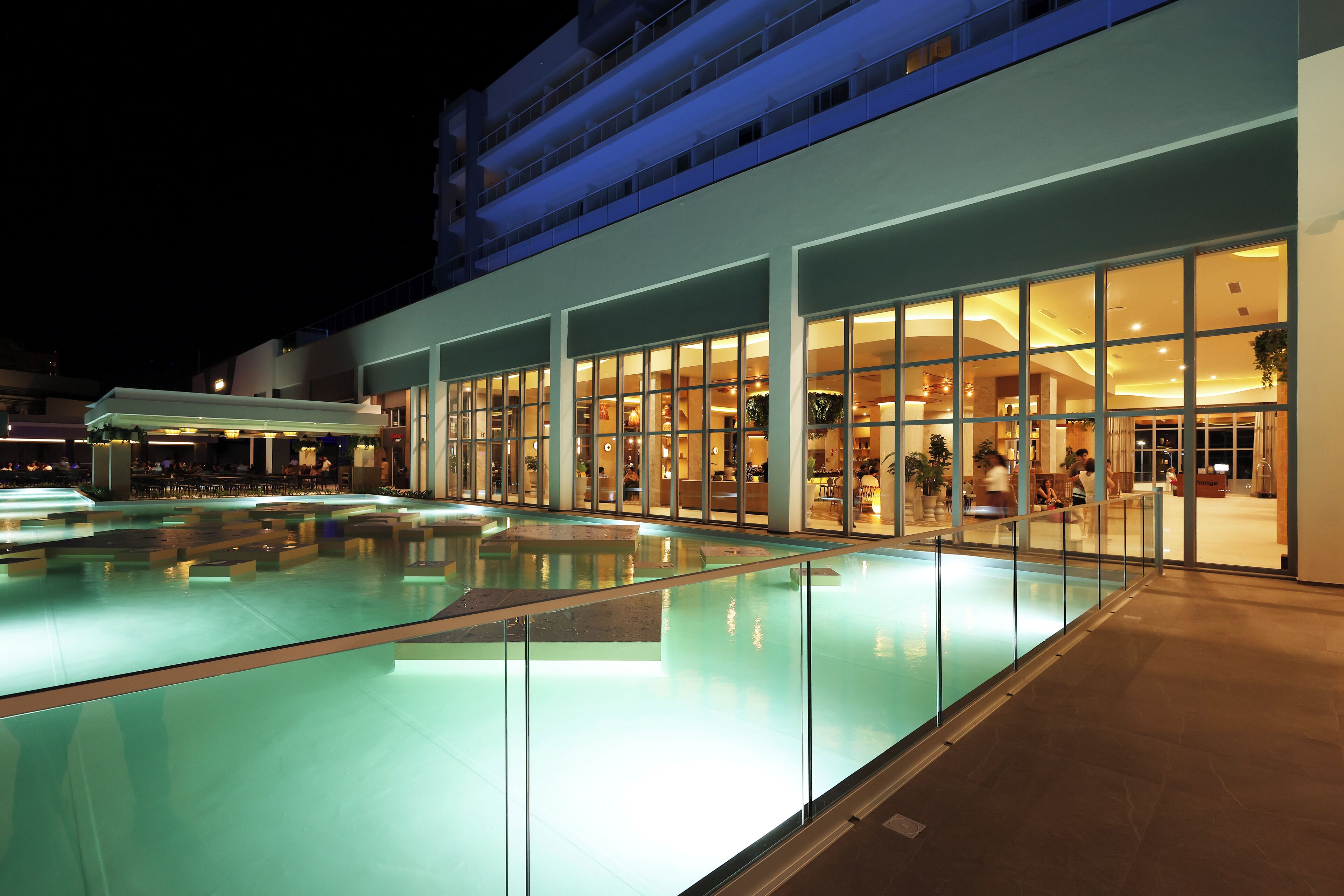 Um hotel moderno com uma grande piscina interior, guarda-corpos de vidro e um átrio bem iluminado.