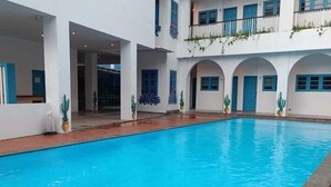 Piscina com deck de madeira, paredes brancas e portas azuis.