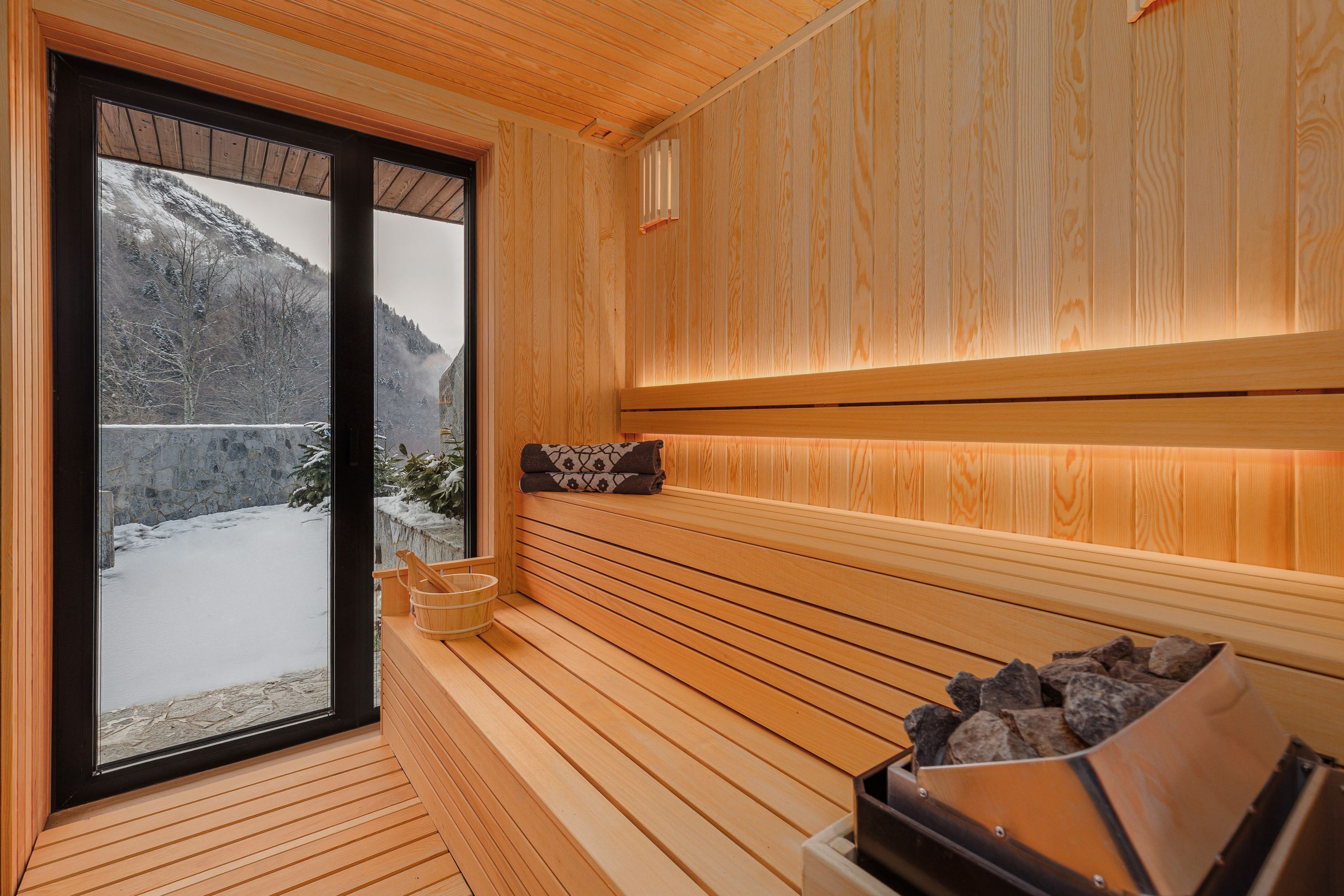 Uma sauna de madeira com um banco, uma janela com vista para montanhas cobertas de neve e uma parede de madeira com um aparelho de luz.