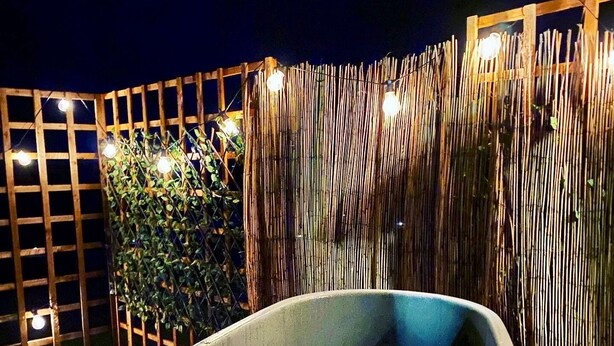 Uma banheira de hidromassagem em área de jardim, com cerca de bambu e treliça de madeira.