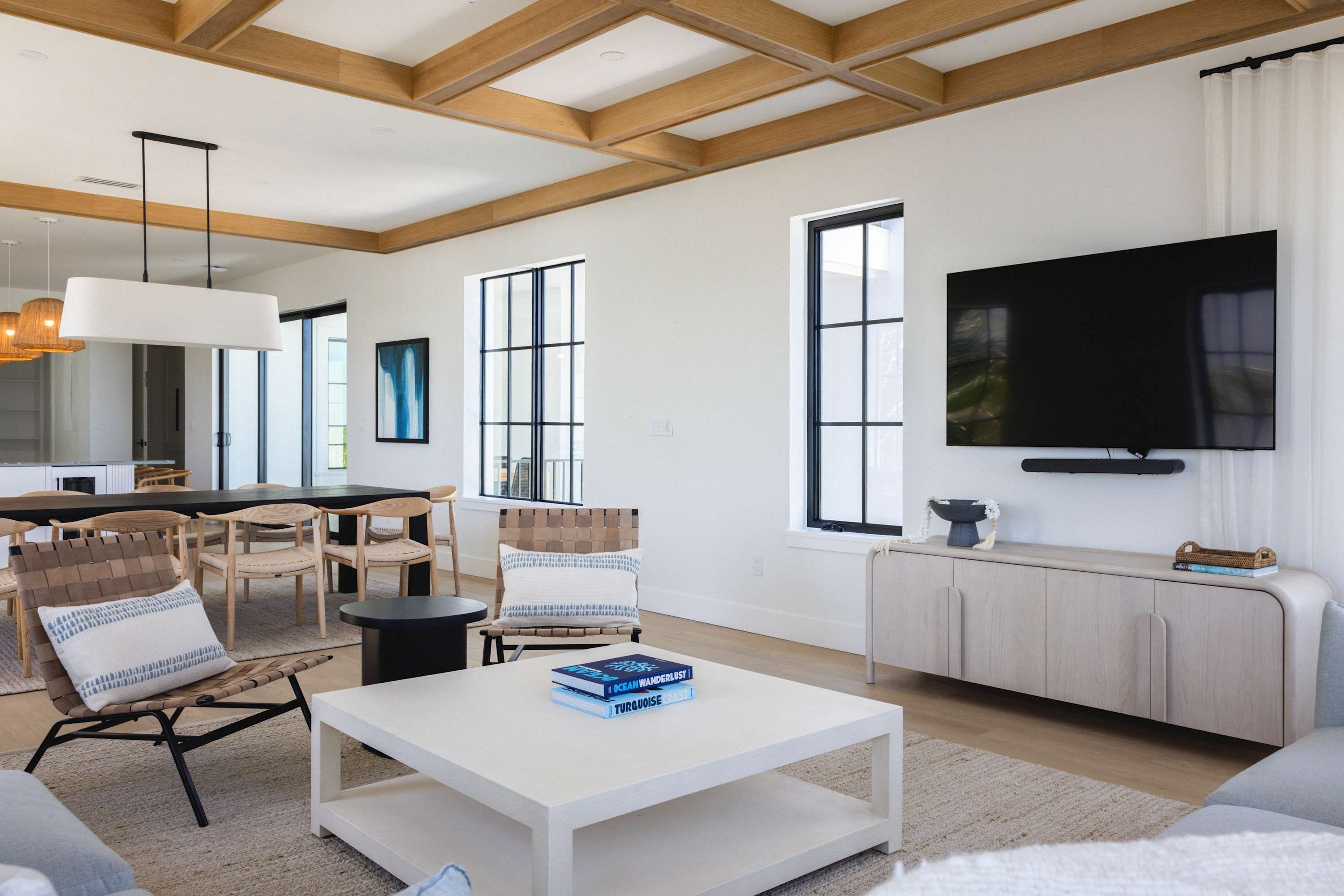 Uma sala de estar moderna com uma mesa de centro branca, uma TV na parede e uma área de jantar com cadeiras de madeira e uma mesa preta.