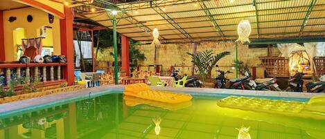 Uma piscina interior com área coberta, assentos e algumas motocicletas estacionadas perto.