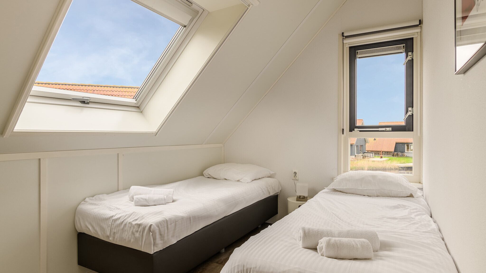 Quarto pequeno e bem iluminado, com duas camas, um claraboia e uma janela com vista para o exterior.