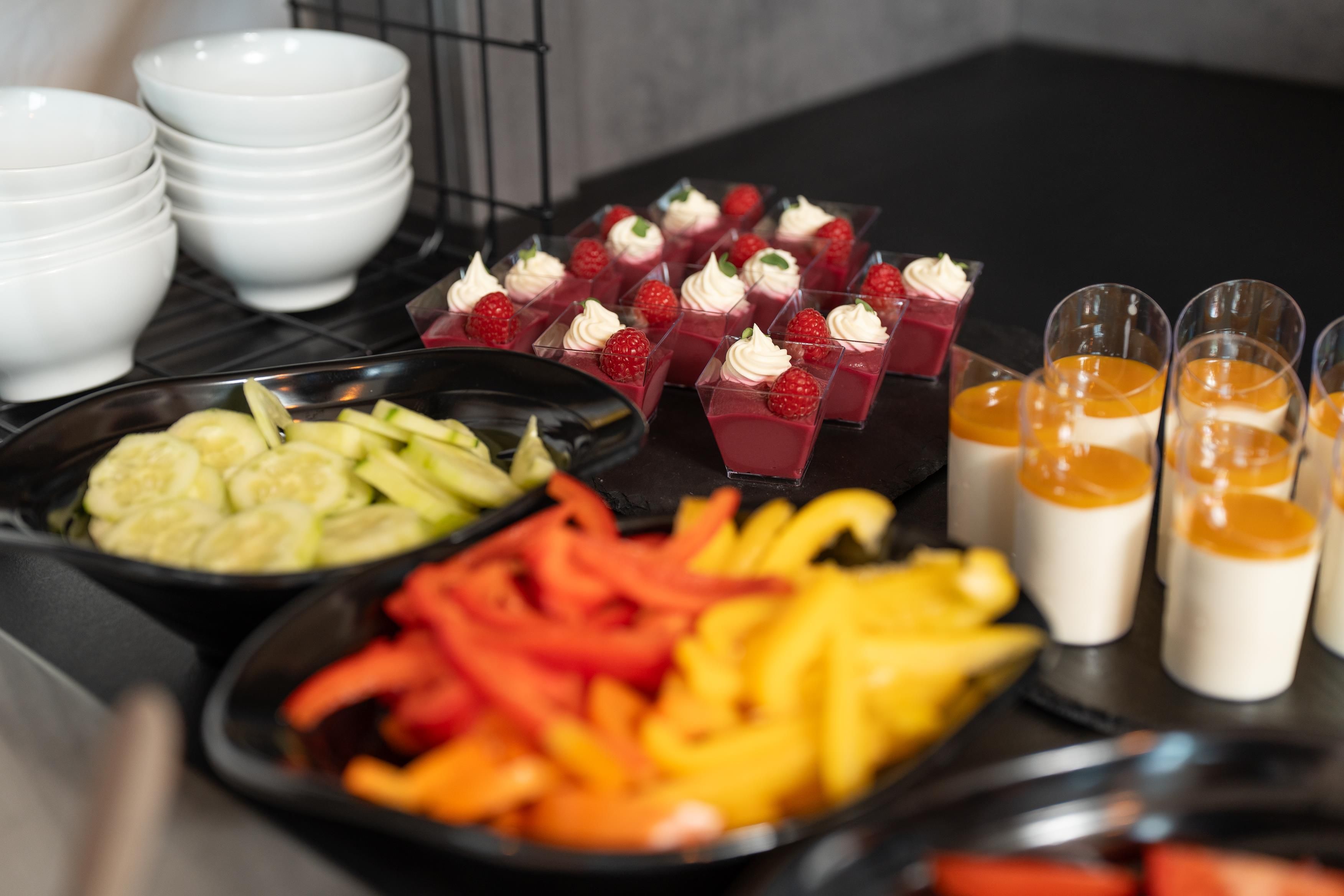 Uma mesa de buffet com diversos alimentos, incluindo legumes fatiados, frutas e sobremesas.