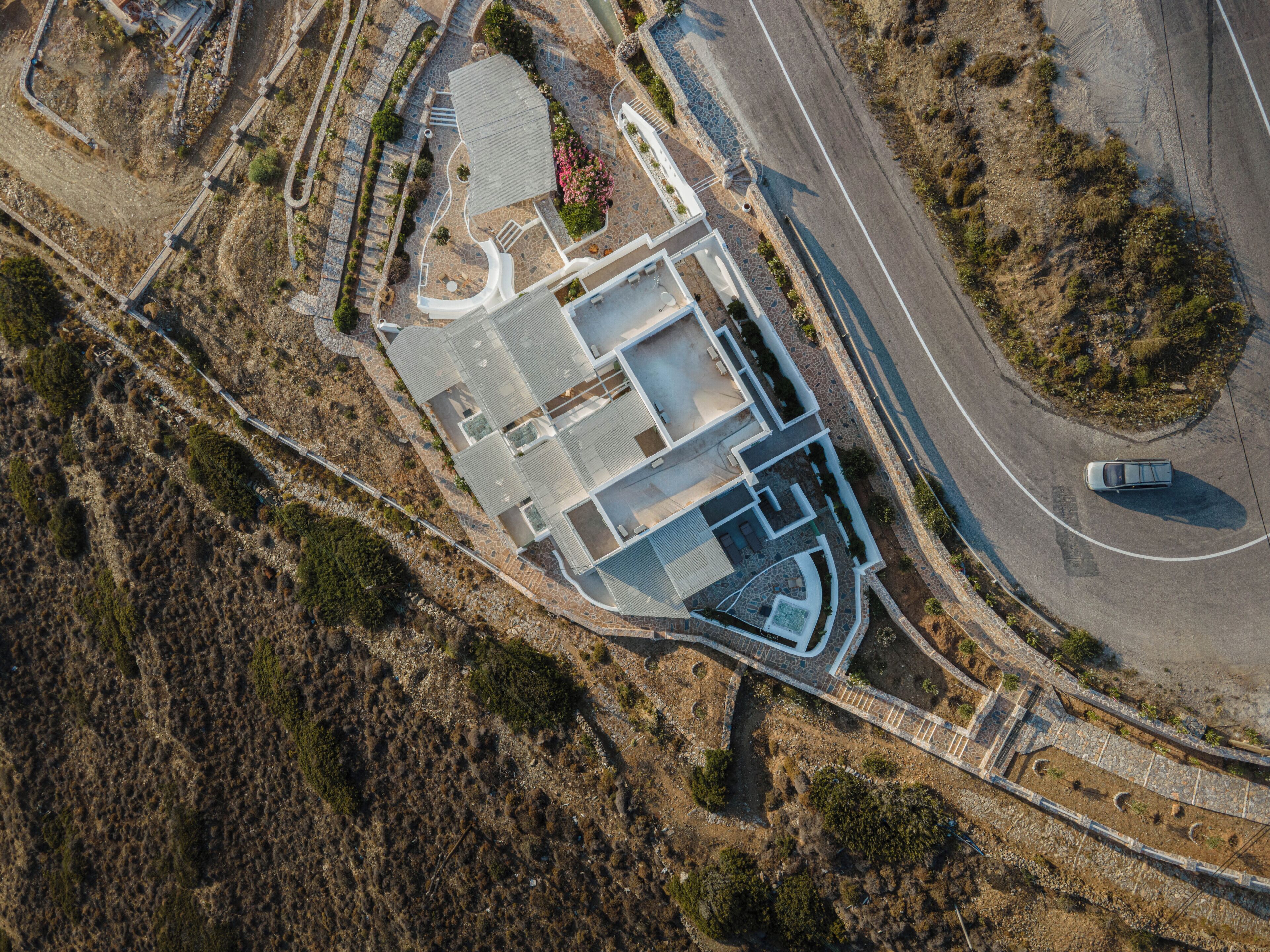 Vista aérea de um edifício moderno com uma entrada curva, área de estacionamento e um jardim ajardinado.