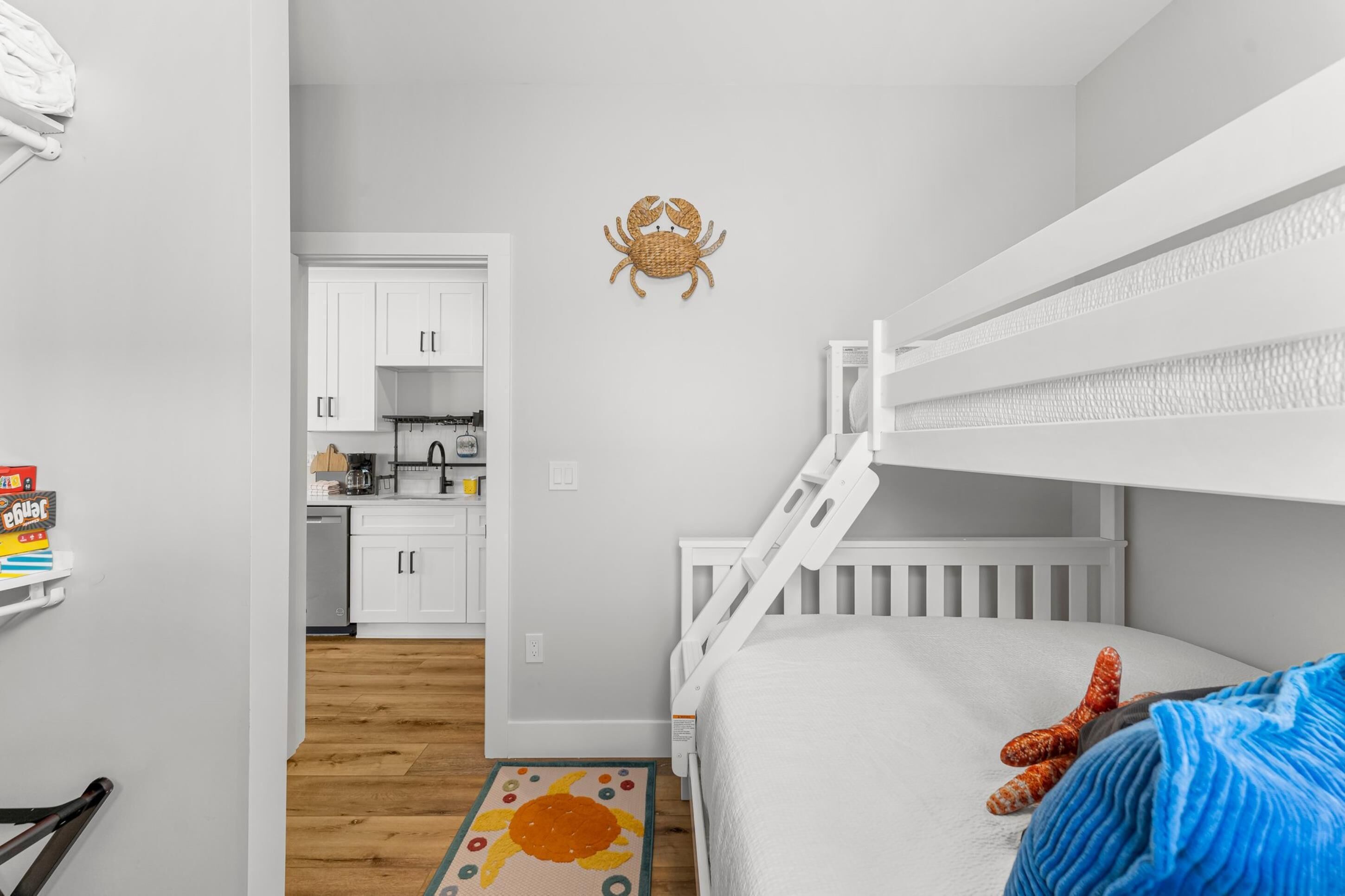 Quarto de criança com beliche, decoração de caranguejo na parede e uma cozinha ao fundo.