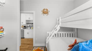 Quarto de criança com beliche, decoração de caranguejo na parede e uma cozinha ao fundo.