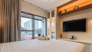 Quarto de hotel com uma cama grande, TV fixada na parede e varanda com vista para a cidade.