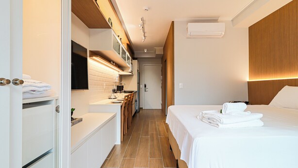 Quarto de hotel com cama, banheiro e cozinha compacta.