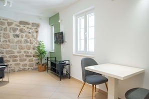 Quarto com parede de pedra, televisão fixada na parede, janela, mesa e uma cadeira.