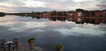 Um lago tranquilo com um cais e cadeiras, cercado por casas e árvores.