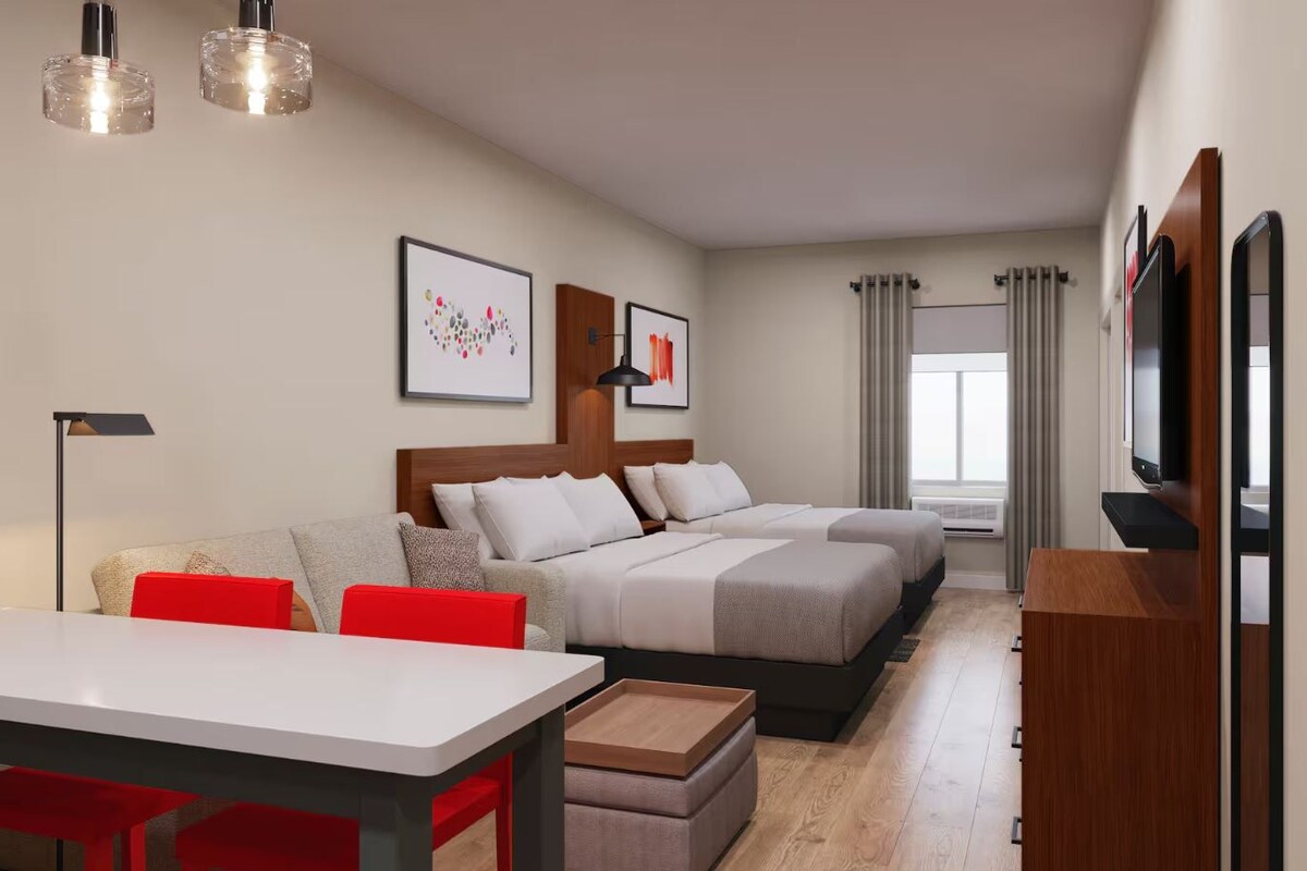 Quarto de hotel moderno com cama, escrivaninha, cadeira, televisão e obras de arte nas paredes.