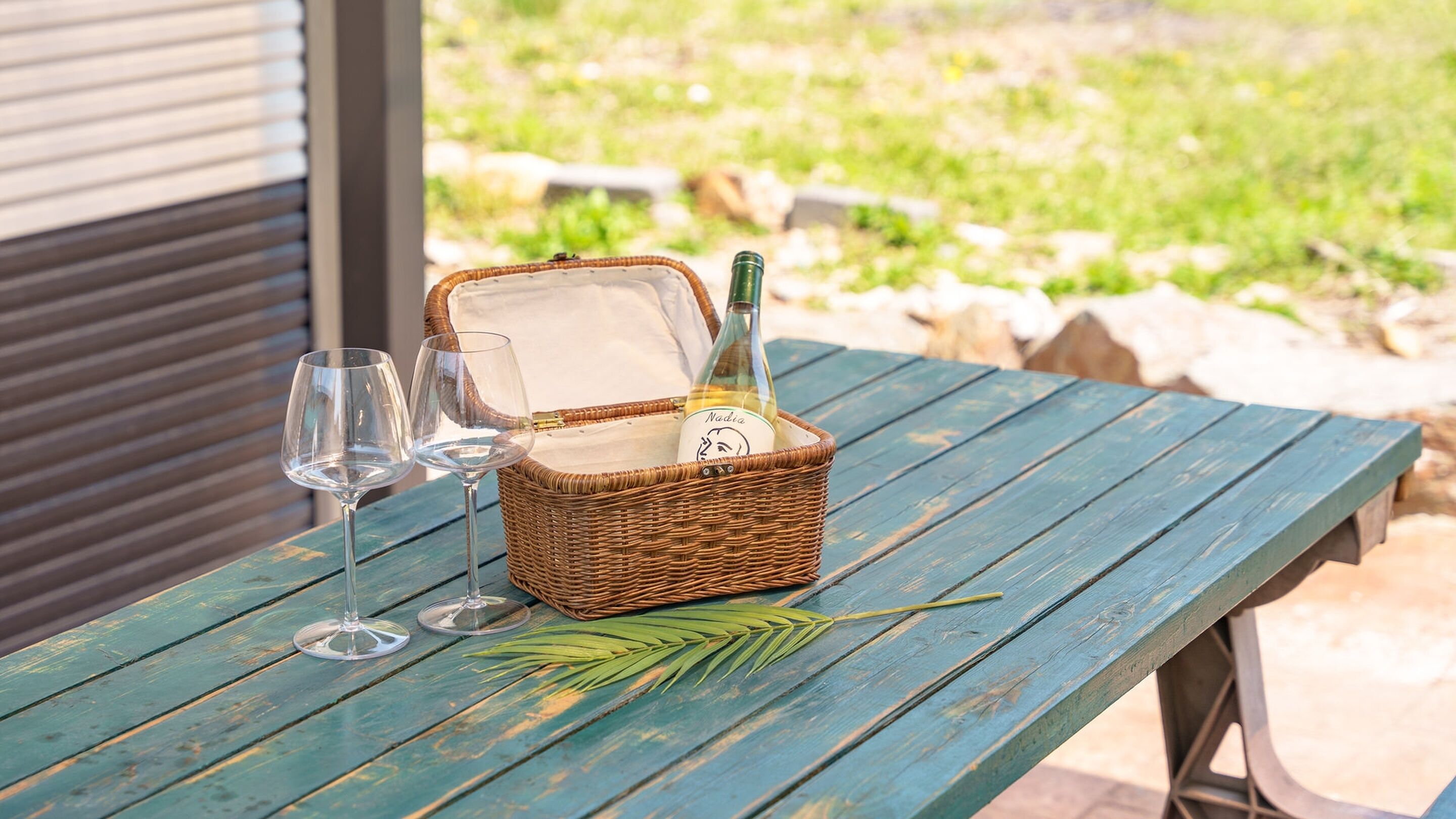 Uma cesta de vime com uma garrafa e dois copos de vinho vazios sobre uma mesa de madeira.