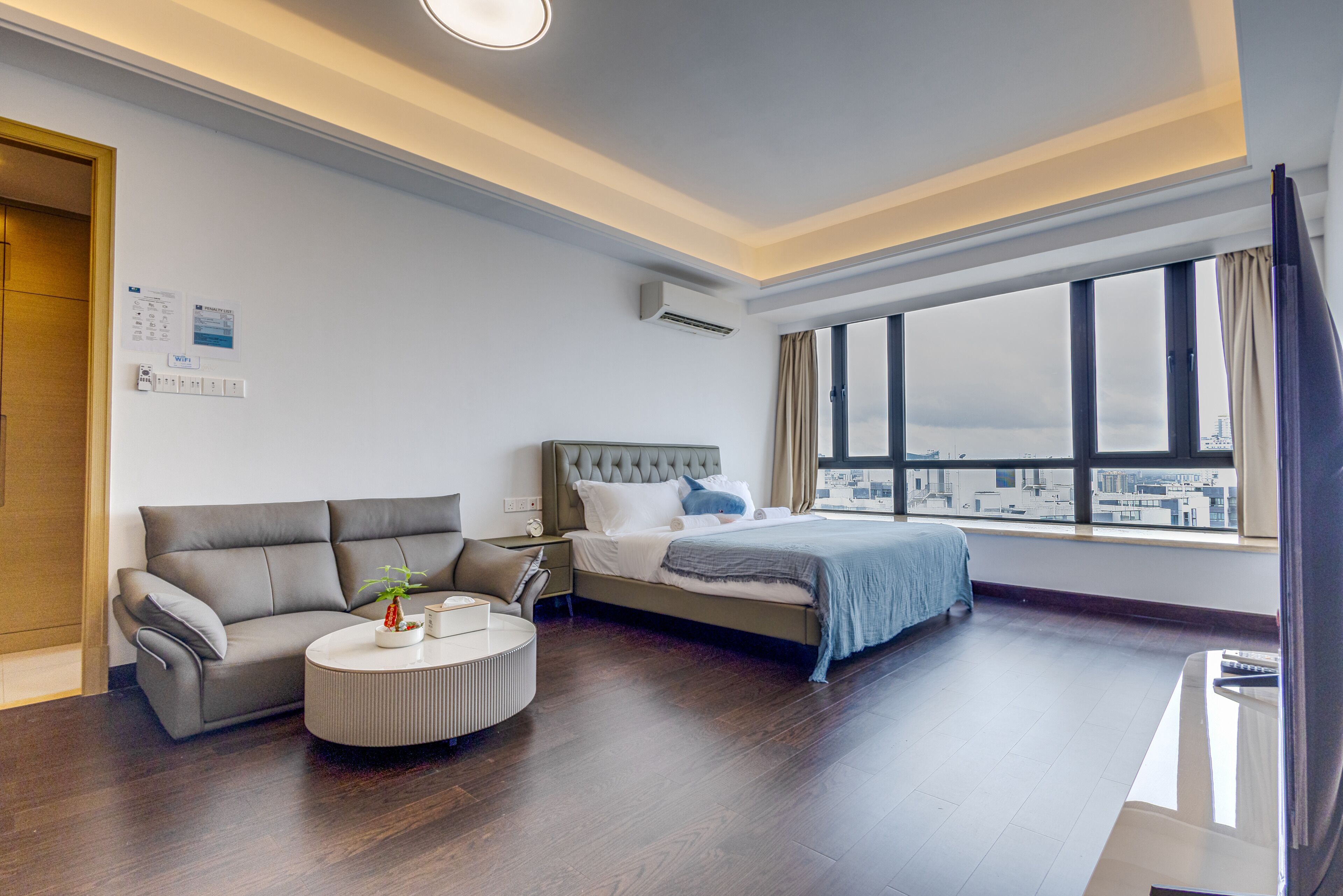 Quarto de hotel moderno com cama, sofá, mesa de centro e uma grande janela com vista para a cidade.