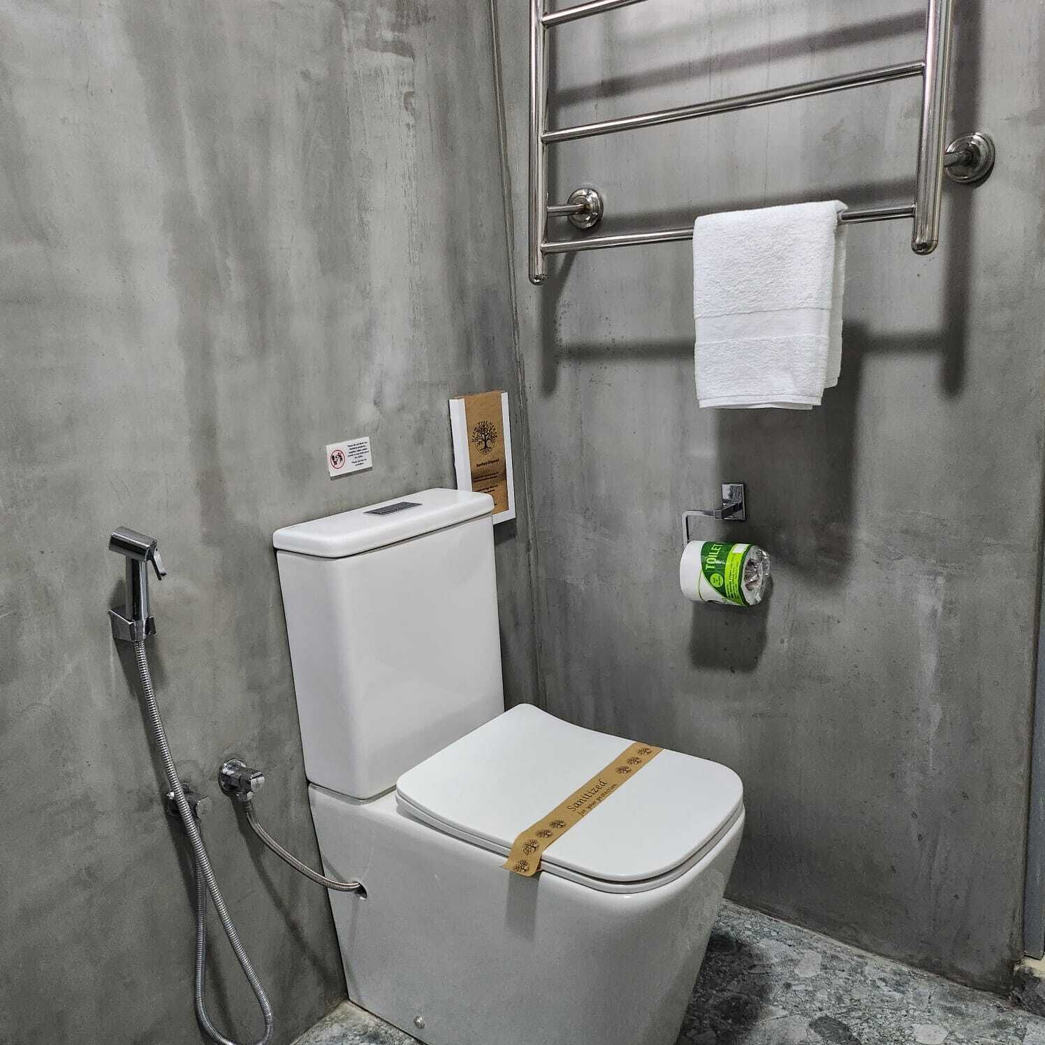 Uma casa de banho compacta e moderna com sanita branca, chuveiro e barra de toalhas.