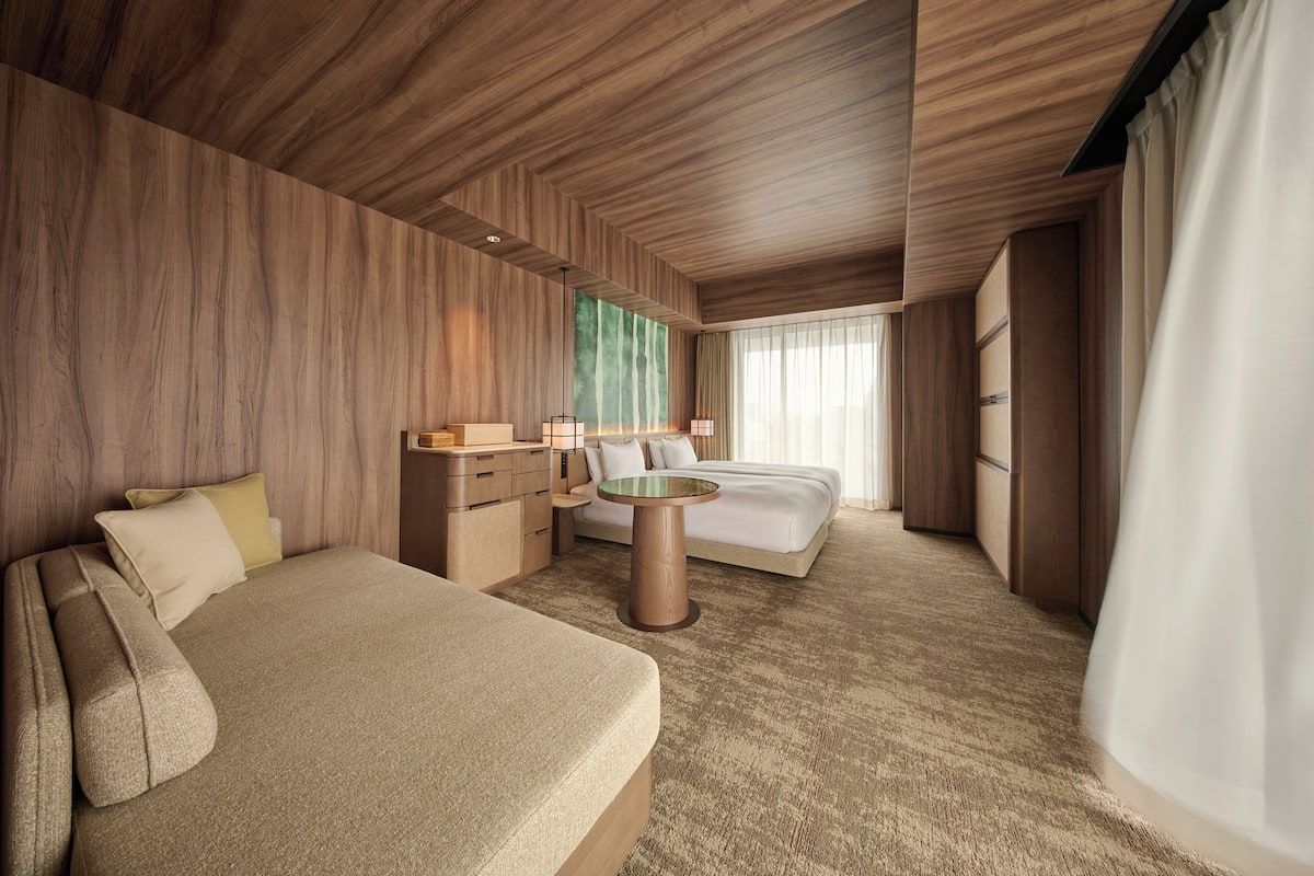 Quarto de hotel com teto de madeira, uma cama, uma mesa pequena e uma mesinha de cabeceira.