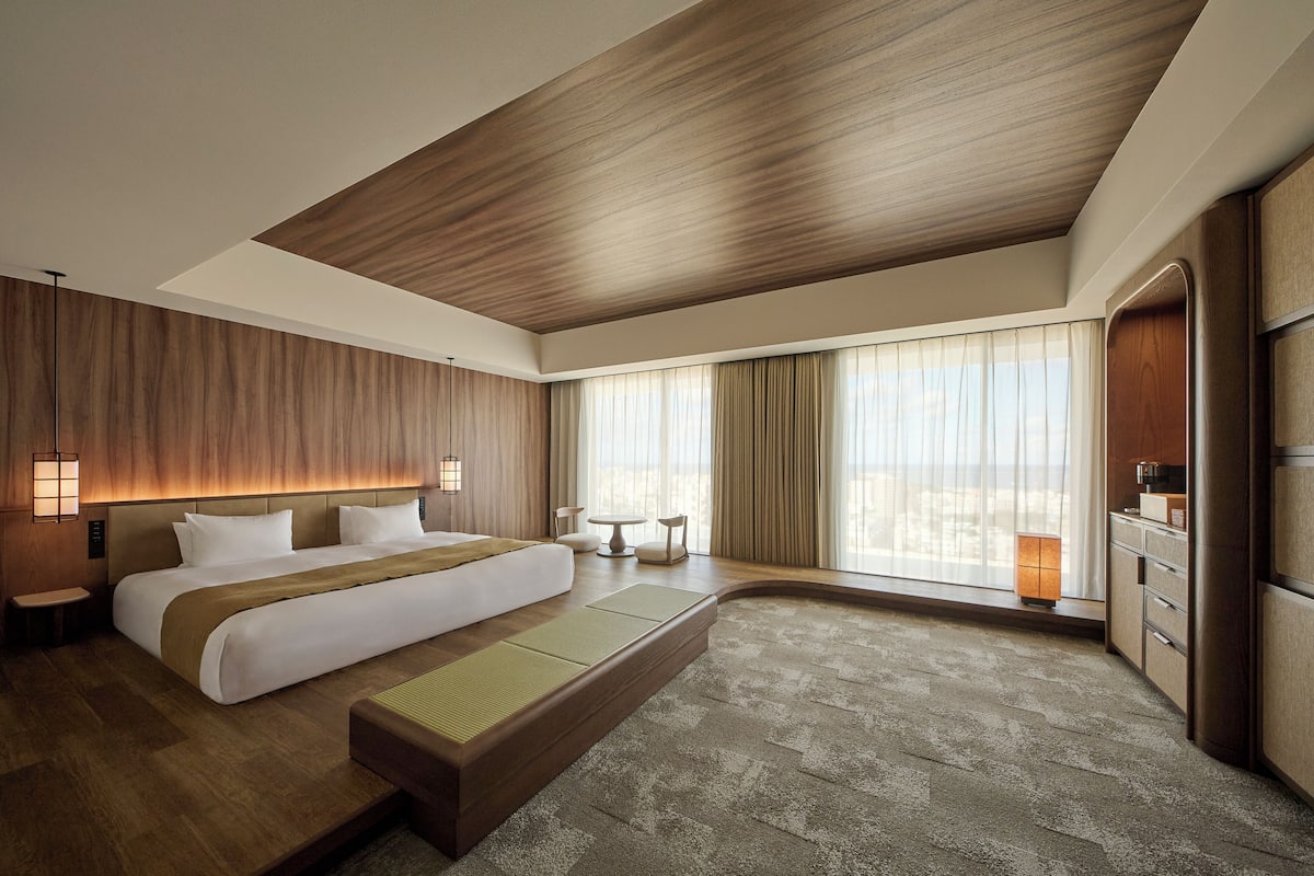 Quarto de hotel moderno com uma cama grande, teto de madeira, escrivaninha e vista para a cidade.