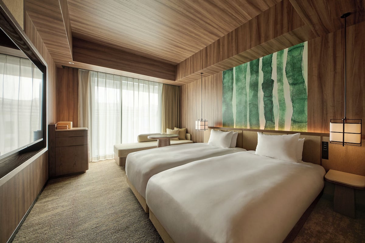 Quarto de hotel com duas camas grandes, um sofá, uma pequena mesa e uma janela ampla com cortinas.
