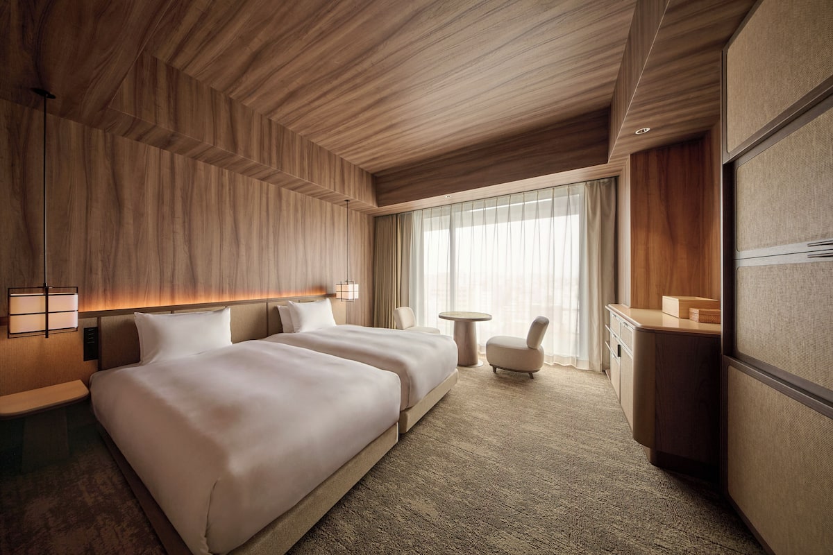 Quarto de hotel com uma cama grande, mesas de cabeceira, escrivaninha e uma cadeira.