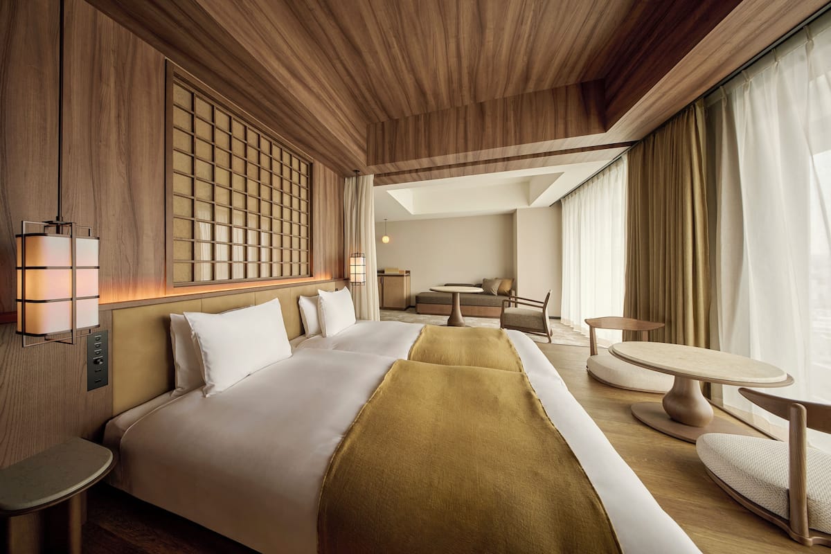 Quarto de hotel com cama grande, mesa de cabeceira, mesa redonda pequena e um sofá.
