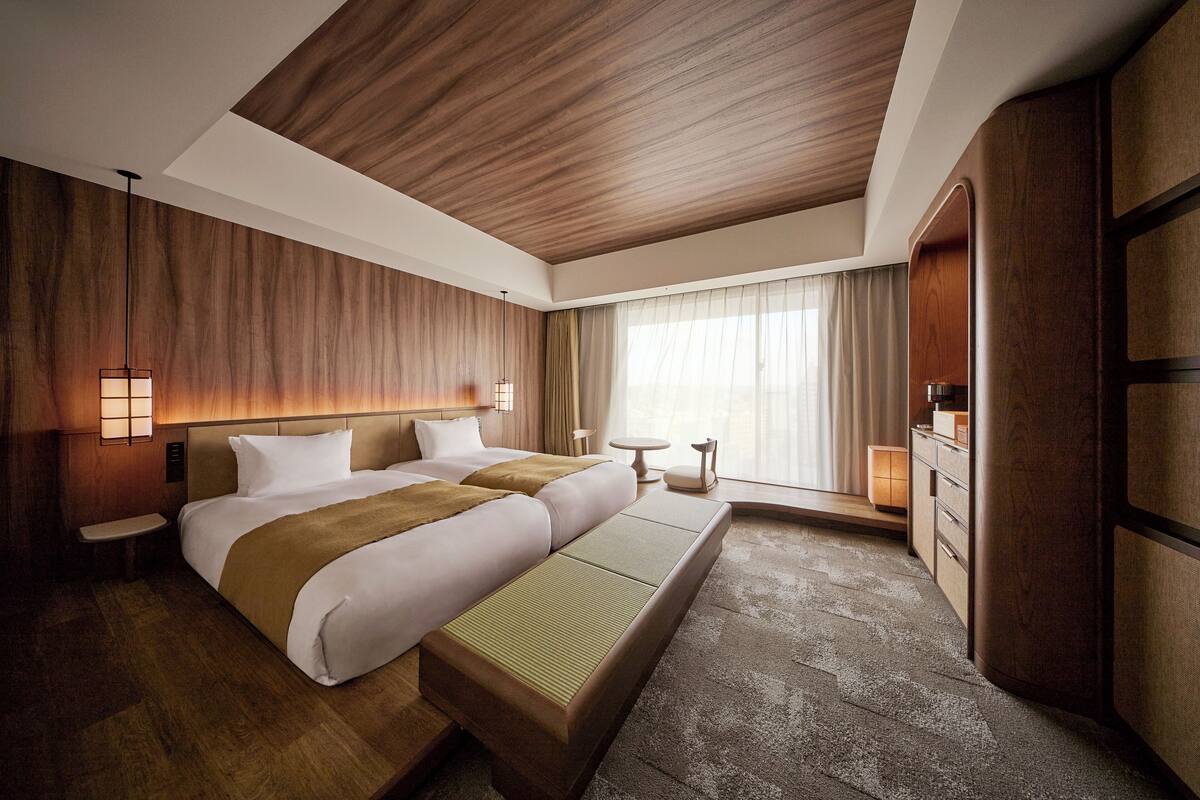 Quarto de hotel moderno com uma cama grande, painéis de madeira, uma escrivaninha e vista para o exterior.