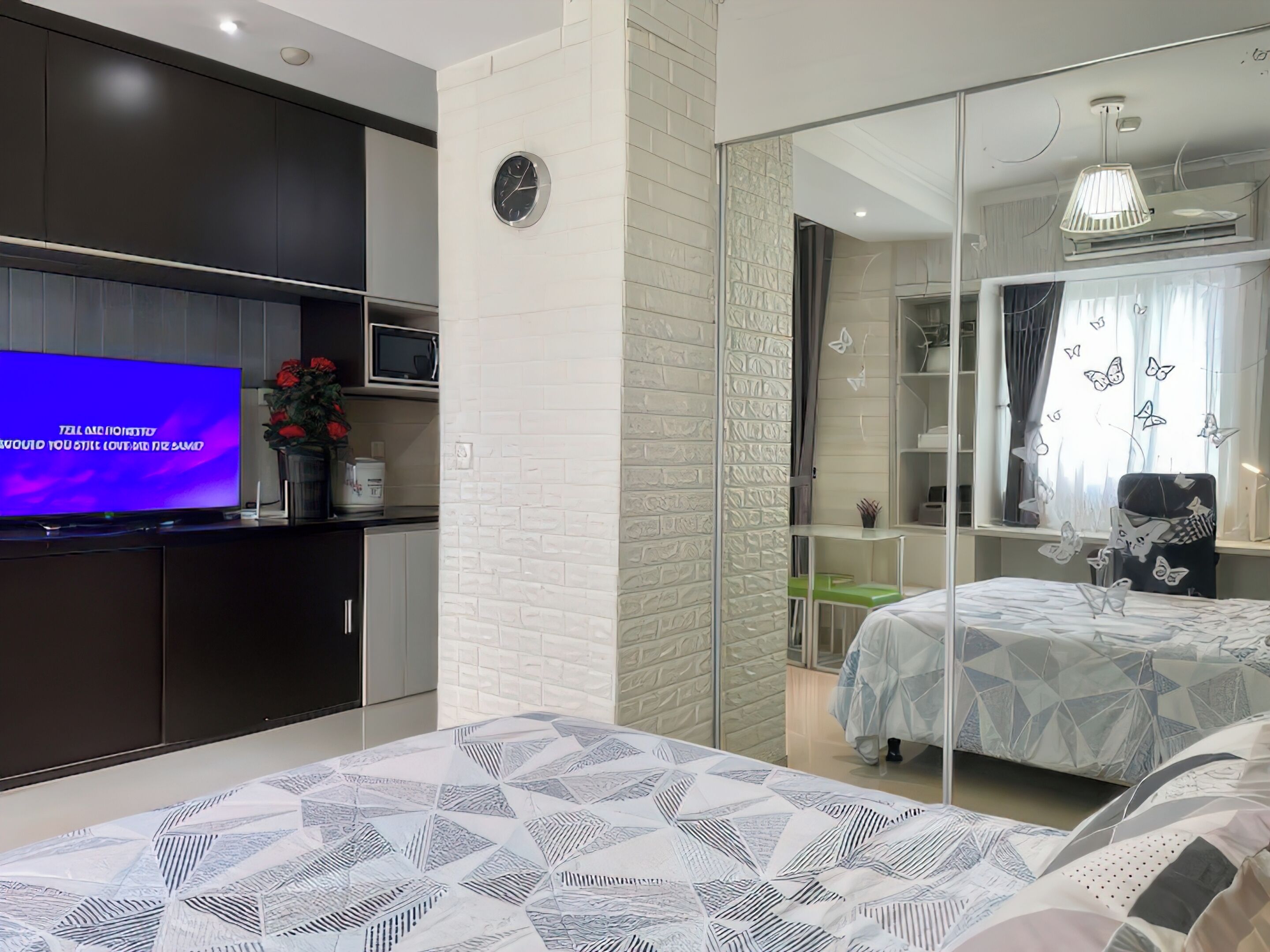Quarto moderno com TV, espelho e duas camas com roupa de cama estampada.