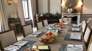 Uma sala de jantar formal com uma longa mesa posta para refeição, exibindo diversos pratos e uma lareira ao fundo.