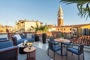 Terraço no telhado com área de estar ao ar livre, vista para uma torre e uma palmeira.