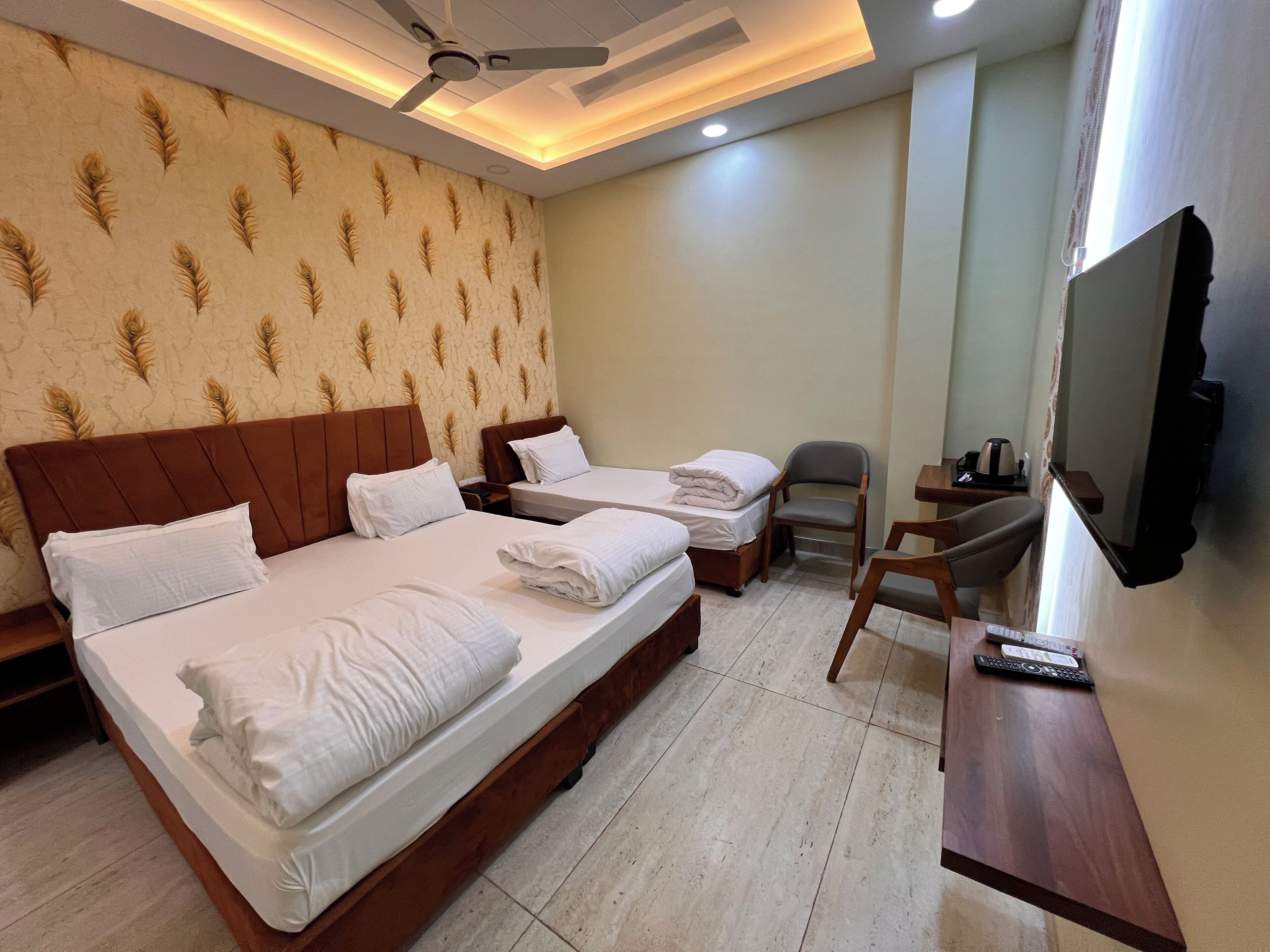 Quarto de hotel com duas camas, ventoinha no teto, televisão e escrivaninha com cadeira.