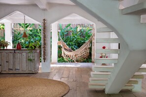 Um quarto amplo com piso de madeira, tapete tecido, rede e escada.