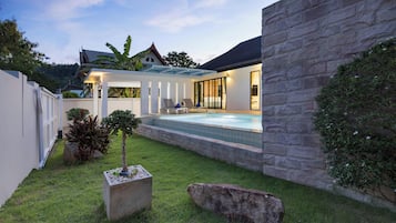 Uma casa moderna com piscina, paredes de pedra e um gramado bem cuidado.