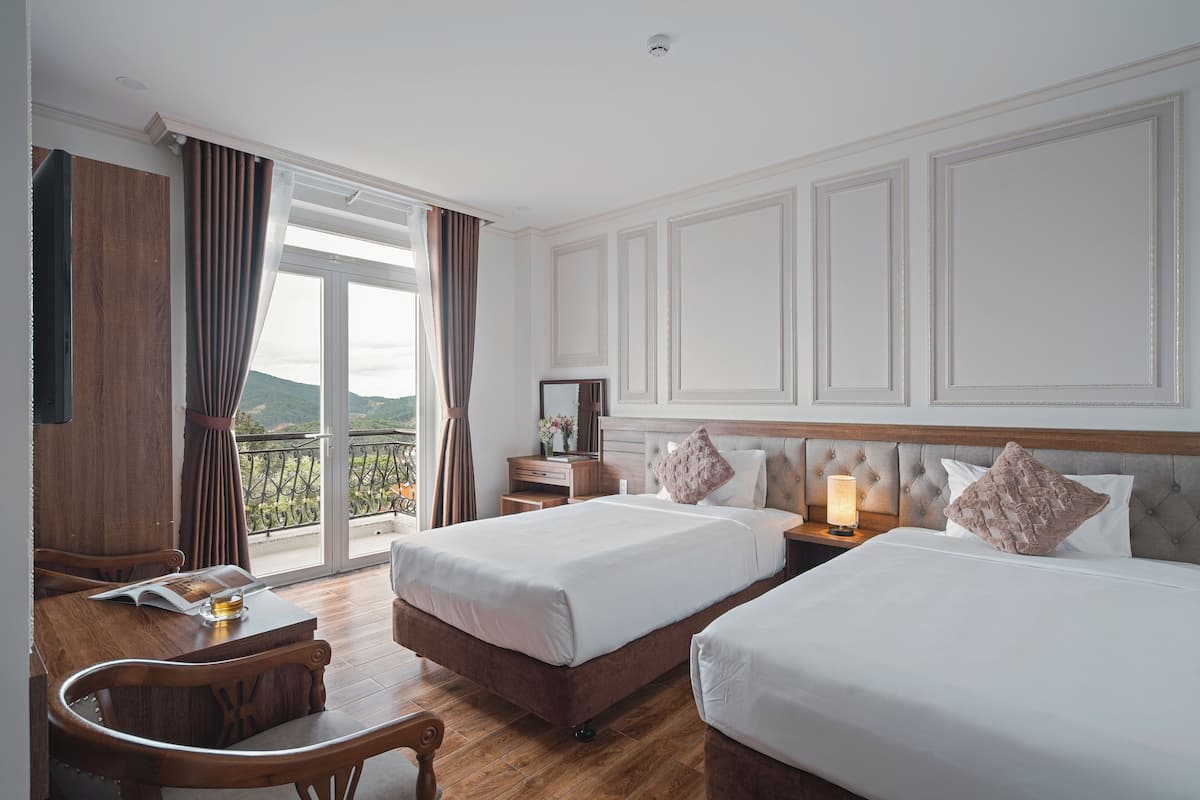 Quarto de hotel com duas camas, uma escrivaninha e vista para o exterior.