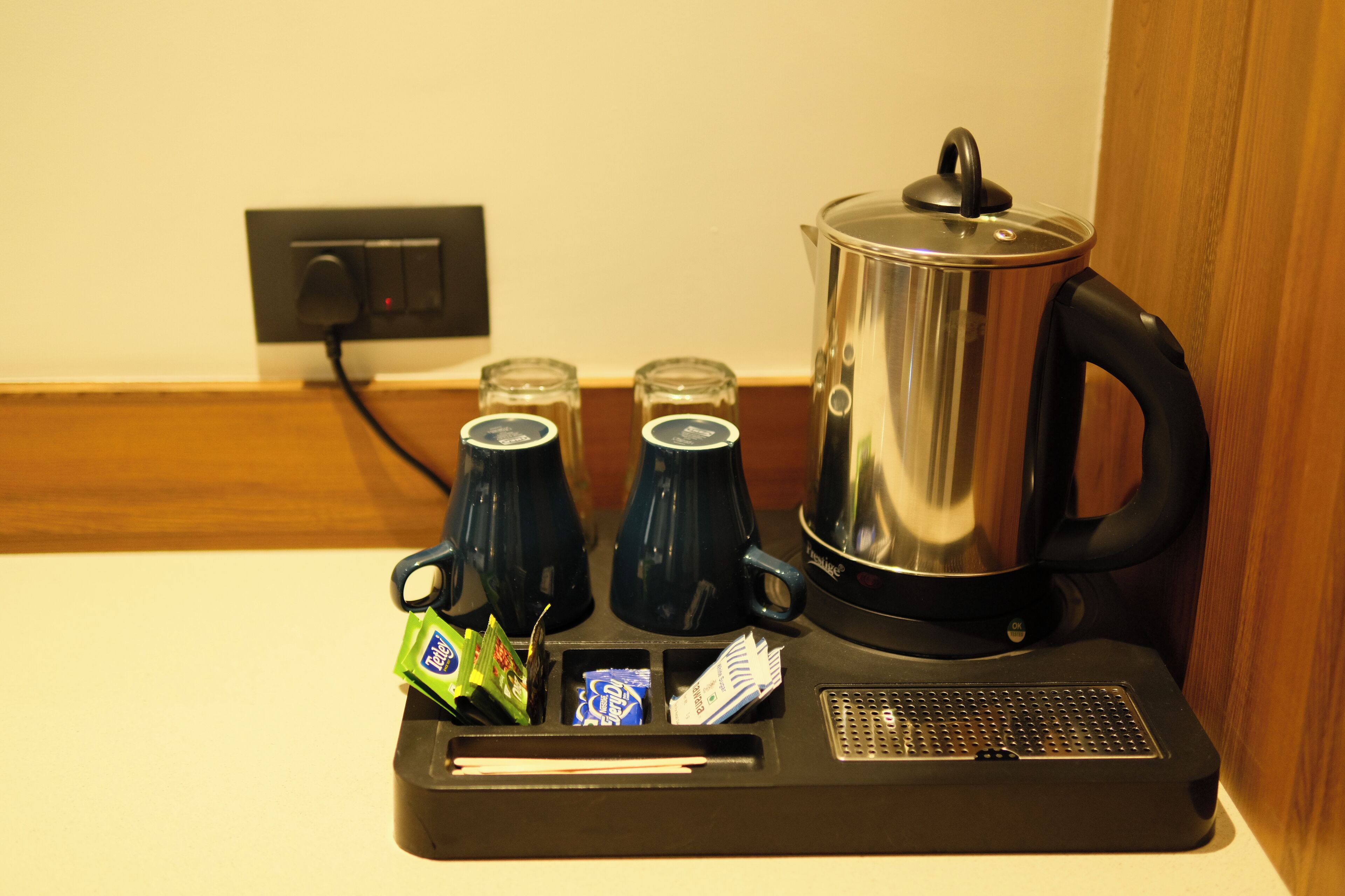 Máquina de café com jarra, duas canecas e um tabuleiro com saquinhos de chá e embalagem.