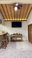 Quarto com teto de madeira, ventilador de teto, televisão na parede, banco de madeira e piso estampado.