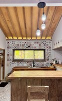 Cozinha com teto de madeira, painel de azulejos, janela com persianas e bancada de madeira.