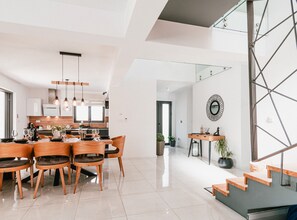 Uma cozinha moderna com armários brancos, uma área de refeições com cadeiras de madeira e uma mesa, e uma escadaria com design geométrico.