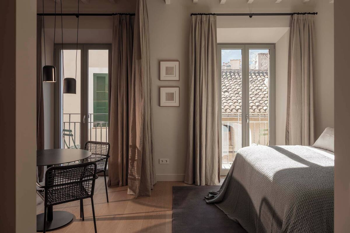 Quarto com cama, escrivaninha com cadeira e varanda com vista.