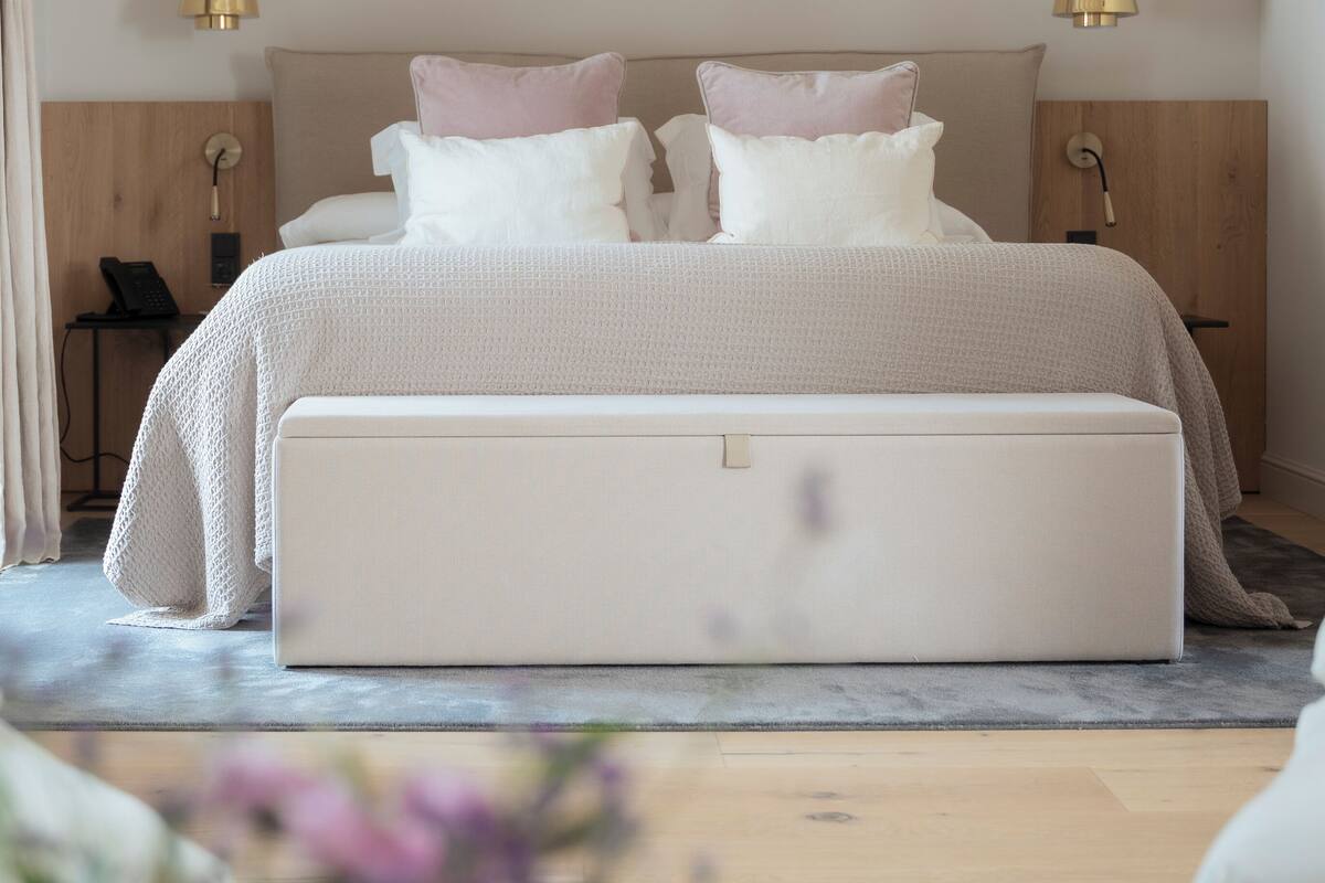 Quarto com cama, mesas de cabeceira e um banquinho.
