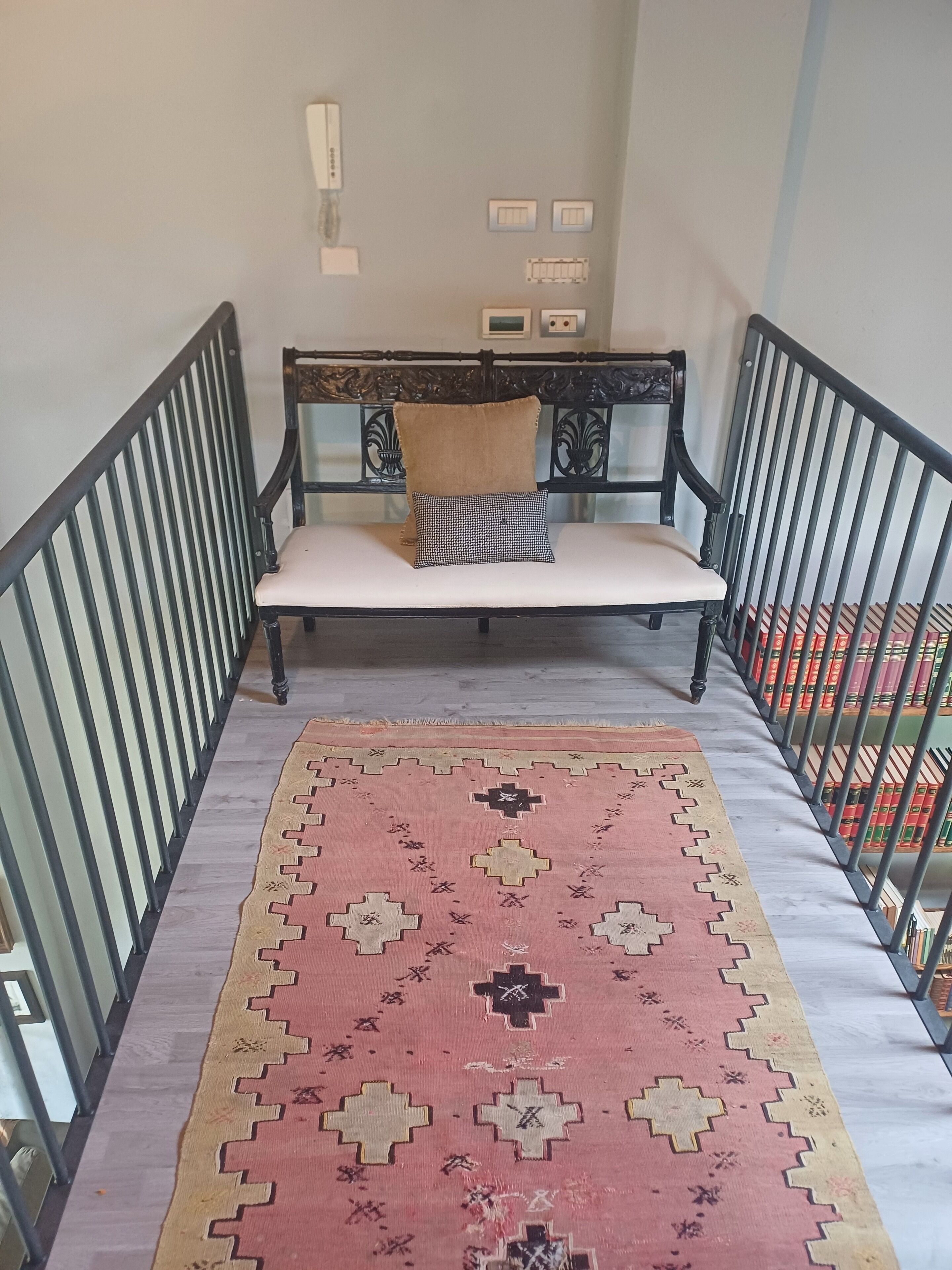 Uma escada com tapete estampado, um banco com almofadas e um corrimão.