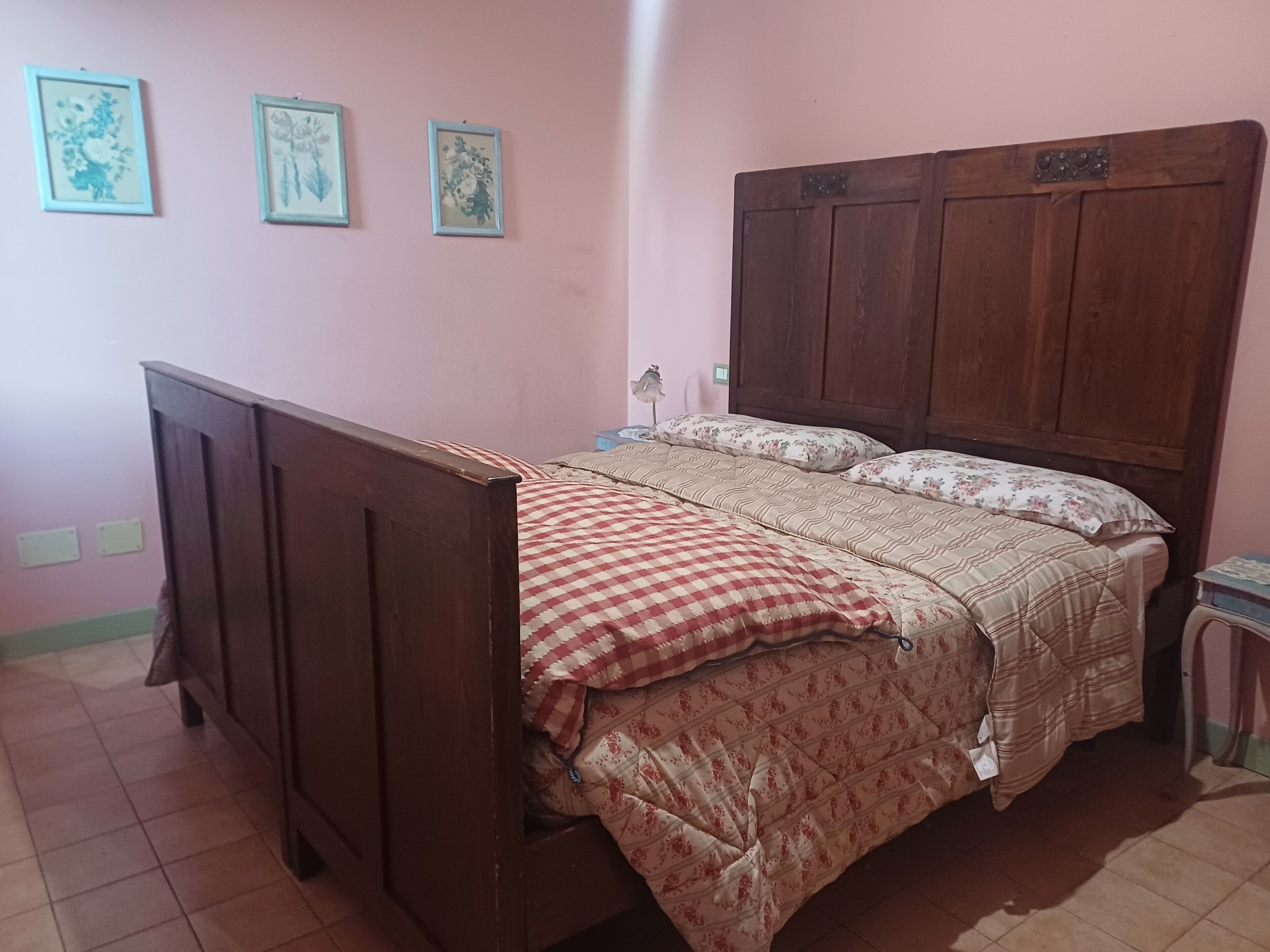 Quarto com cama de madeira, roupa de cama florida e três quadros na parede.