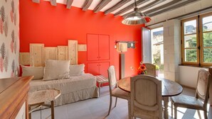 Quarto com parede vermelha, uma cama, uma mesa de jantar com cadeiras e uma janela com vista para vegetação.
